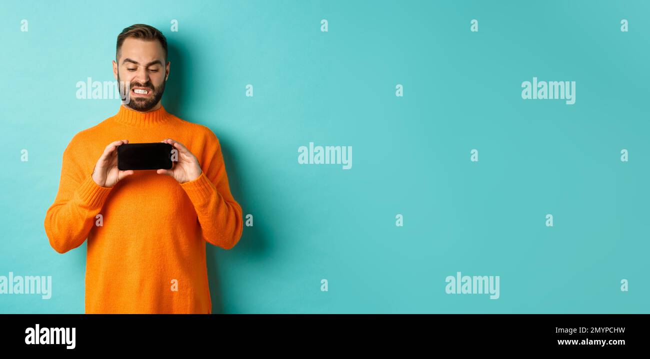 Image of man cringe at something on mobile screen, staring disgusted at ...