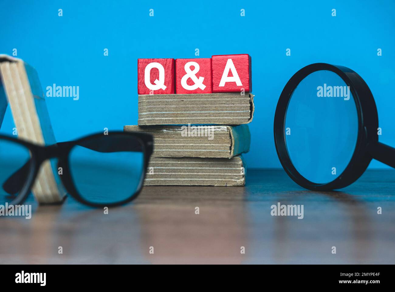 A magnifying glass, glasses ,a stack of book and red wooden cube ...