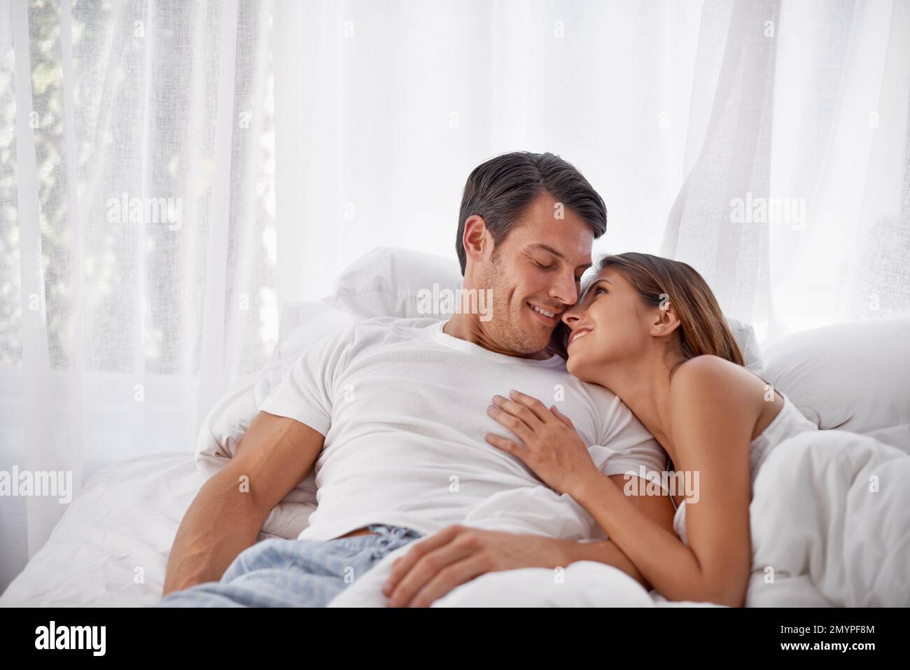 Love, couple and cuddle in bed, relationship and happiness on Valentines day, embrace and ...
