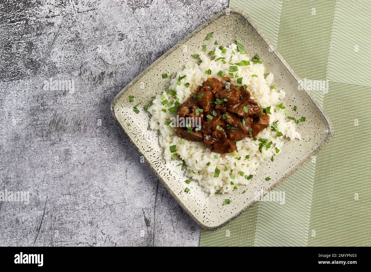 Pork stew with rice and herbs on a square plate on a dark background ...