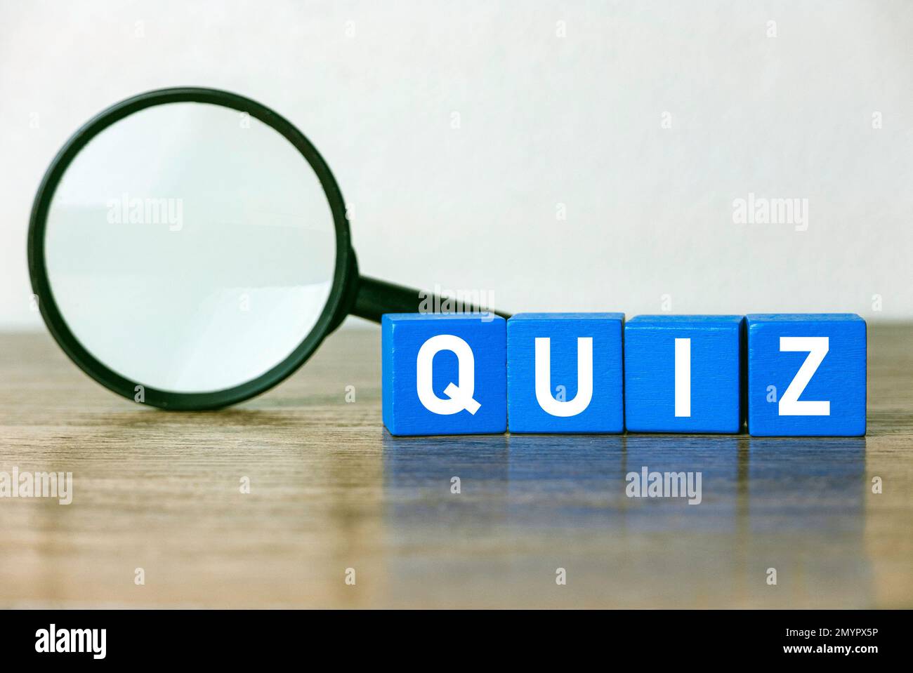 A magnifying glass and a blue wooden cube written with QUIZ on a table ...