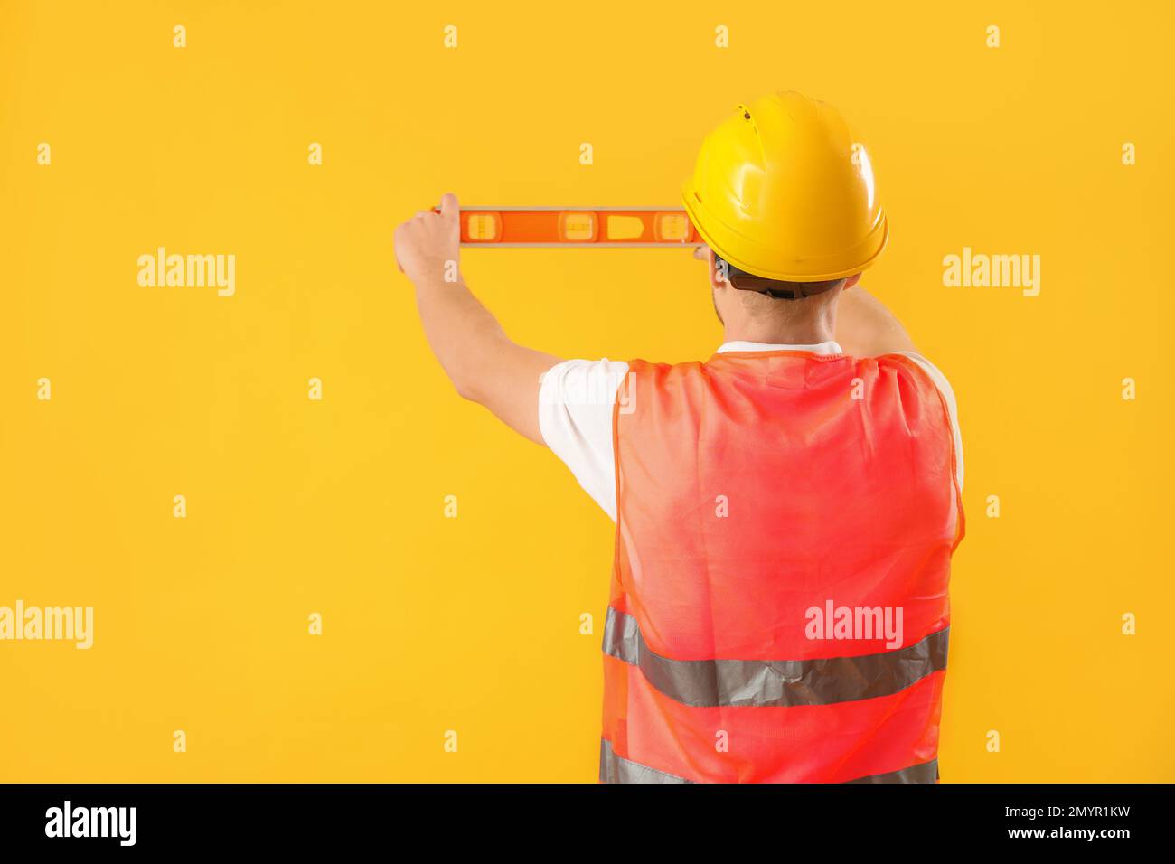 Male worker with builder's level on yellow background Stock Photo - Alamy