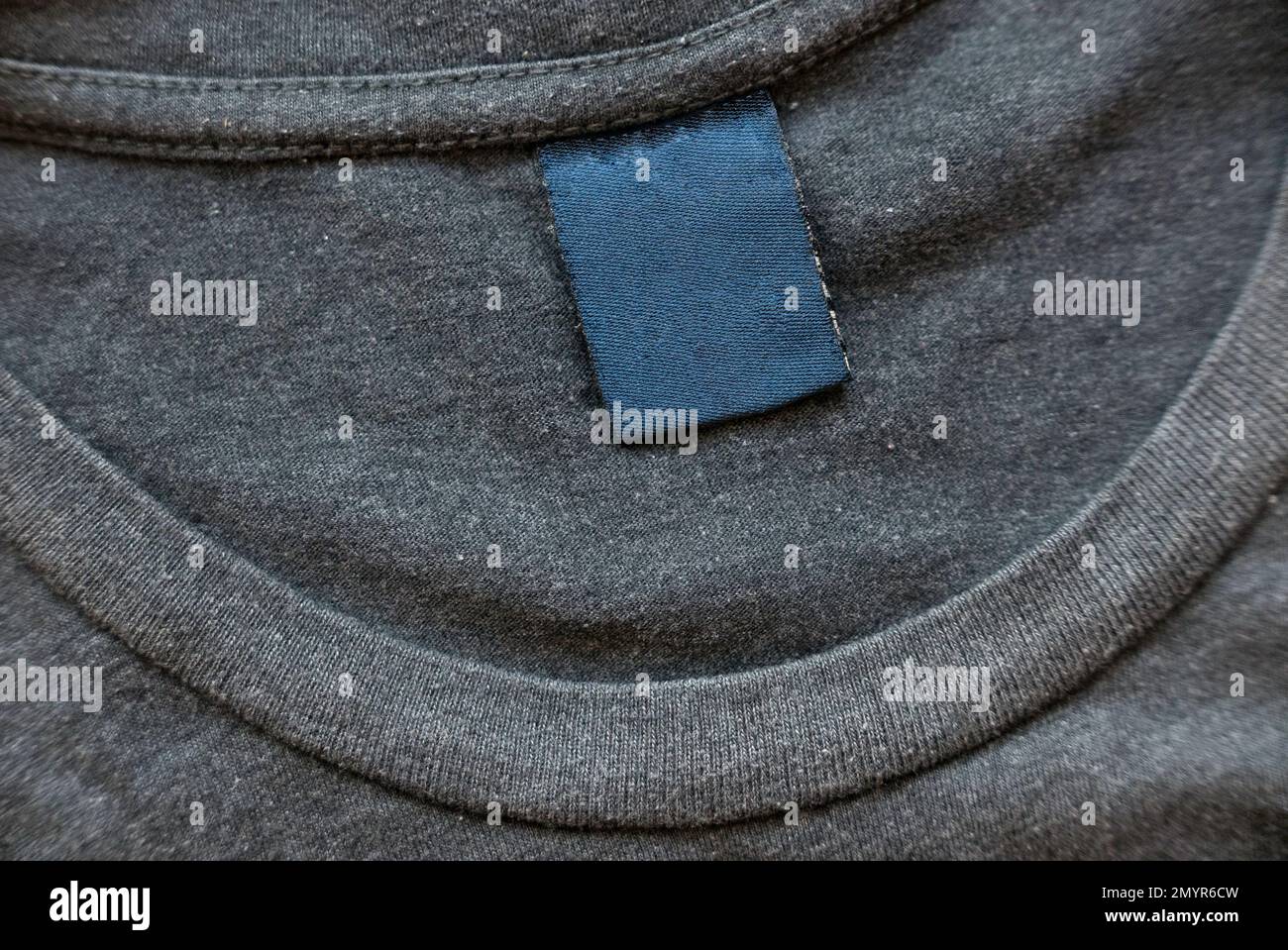 Blank blue laundry care clothes label on grey fabric texture background ...