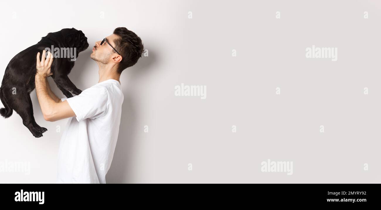 Profile of handsome young man kissing small cute dog face. Hipster guy ...