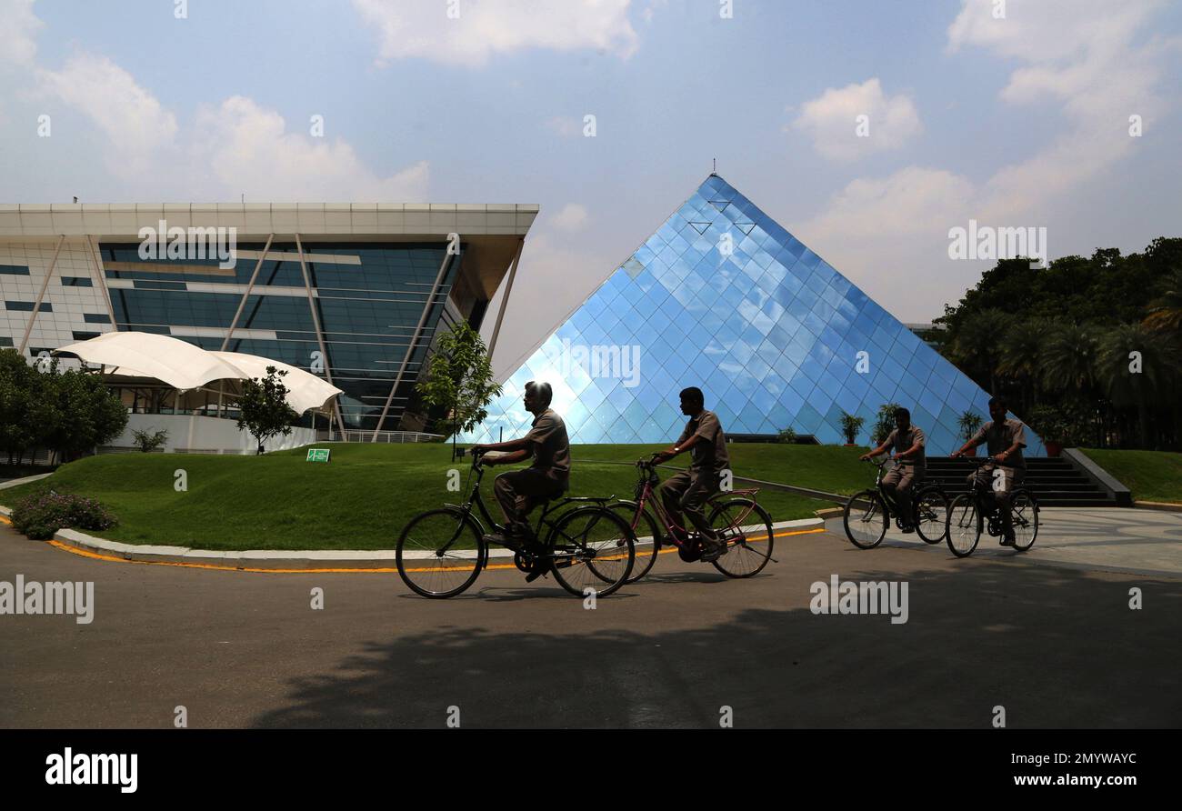 Infosys gardening staff ride bicycles past a pyramid shaped building at ...