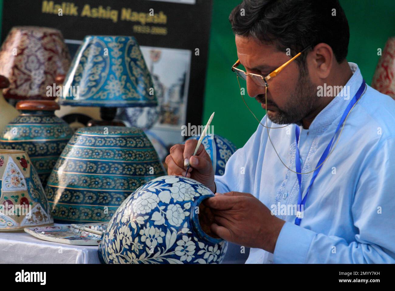 An artist paints traditional designs on a vase inside his stall during ...