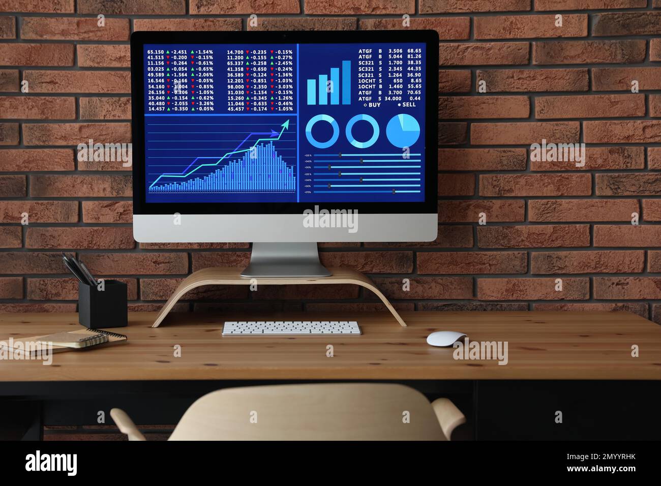 Modern computer with statistic information on wooden table near brick ...