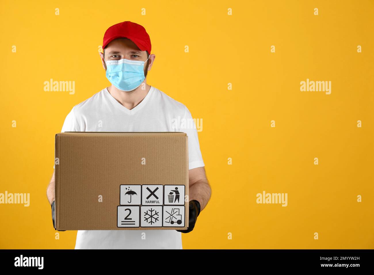 Courier in mask holding cardboard box with different packaging symbols ...