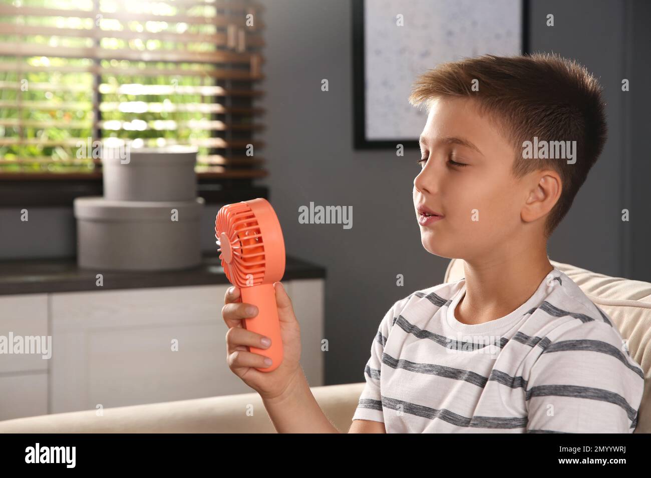 Little boy enjoying air flow from portable fan at home. Summer heat ...