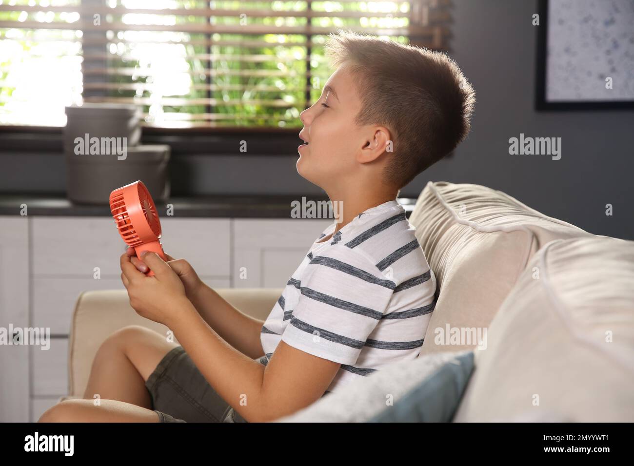 Little boy enjoying air flow from portable fan at home. Summer heat ...