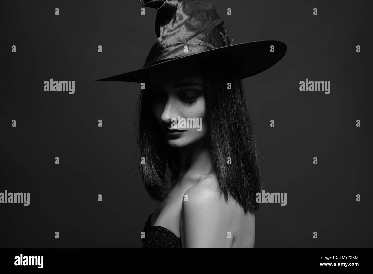 Mysterious witch wearing hat on dark background. Black and white effect ...