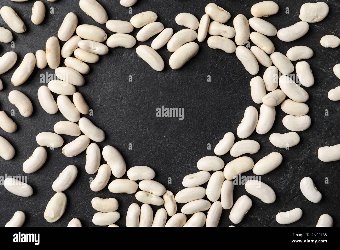 Heart shaped frame made of raw beans on black background, flat lay with ...