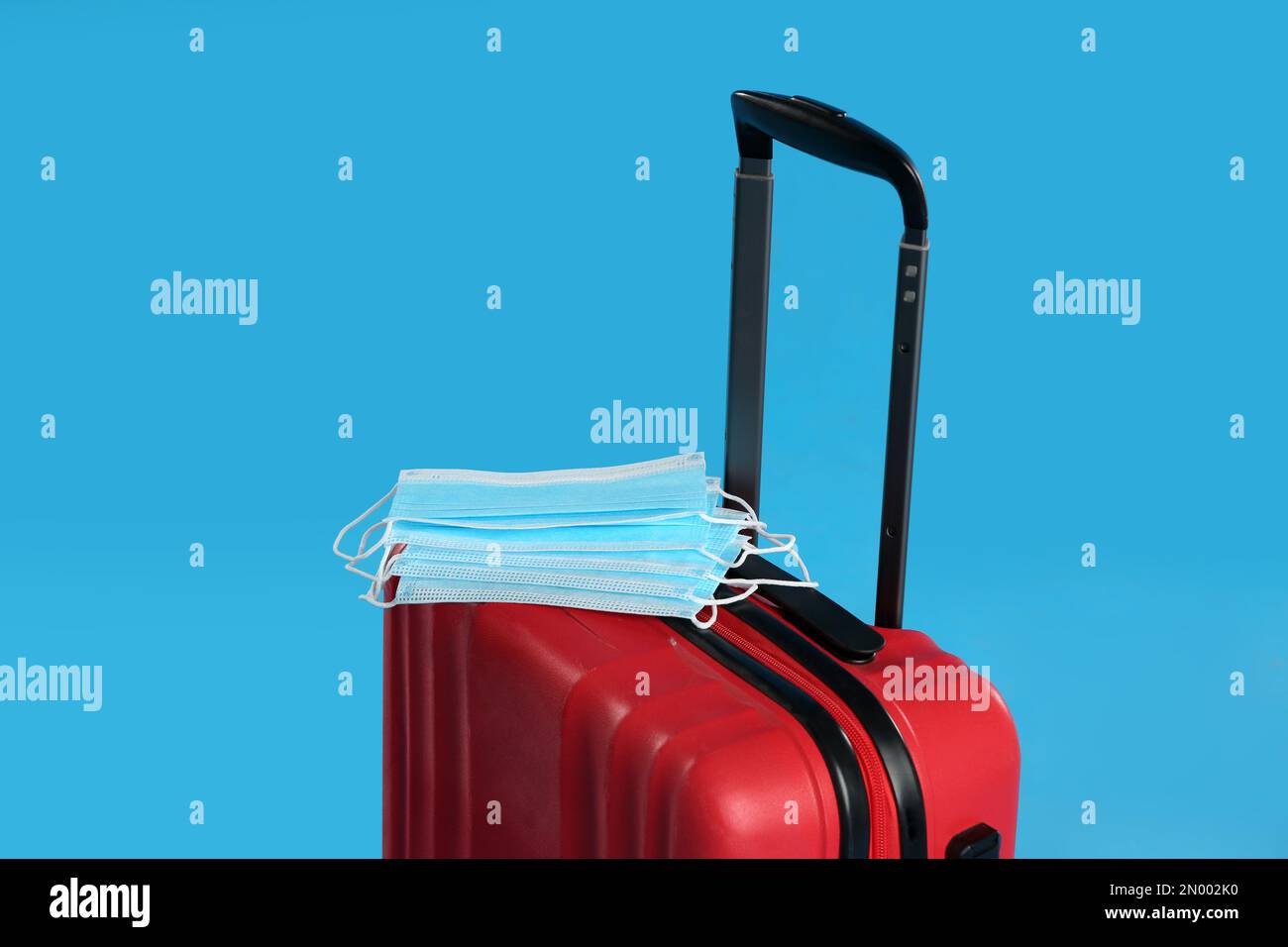 Stylish red suitcase and protective masks on light blue background ...