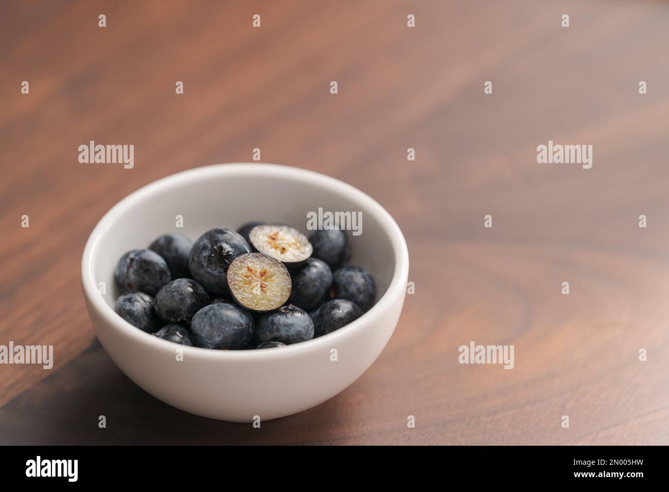 Fresh blueberries in white bowl one berry is cut in halves, shallow ...