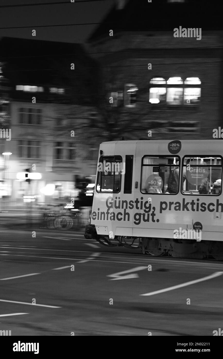 A grayscale of a tram going through town streets at night on the street ...