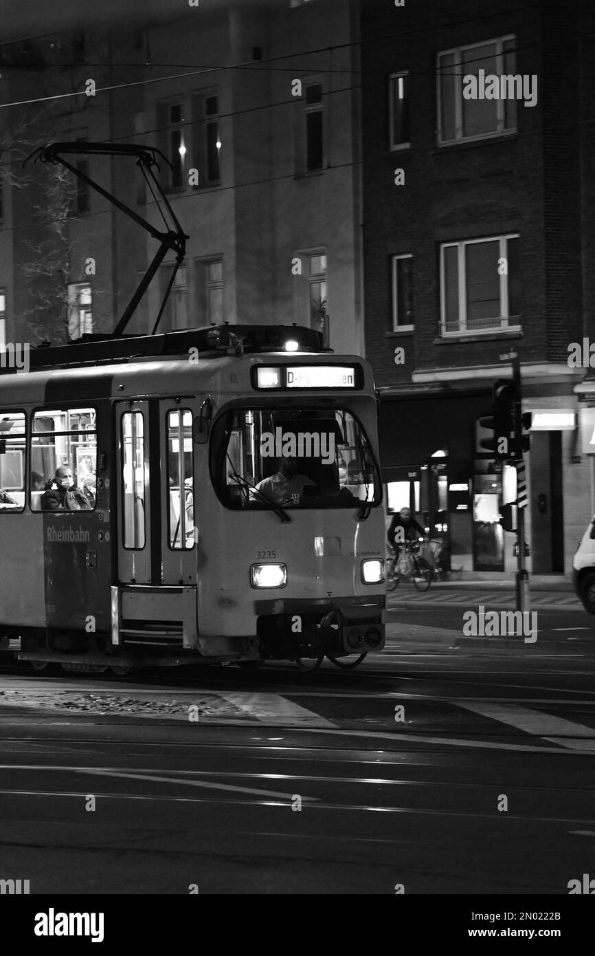 A grayscale of a tram going through town streets at night on the street ...