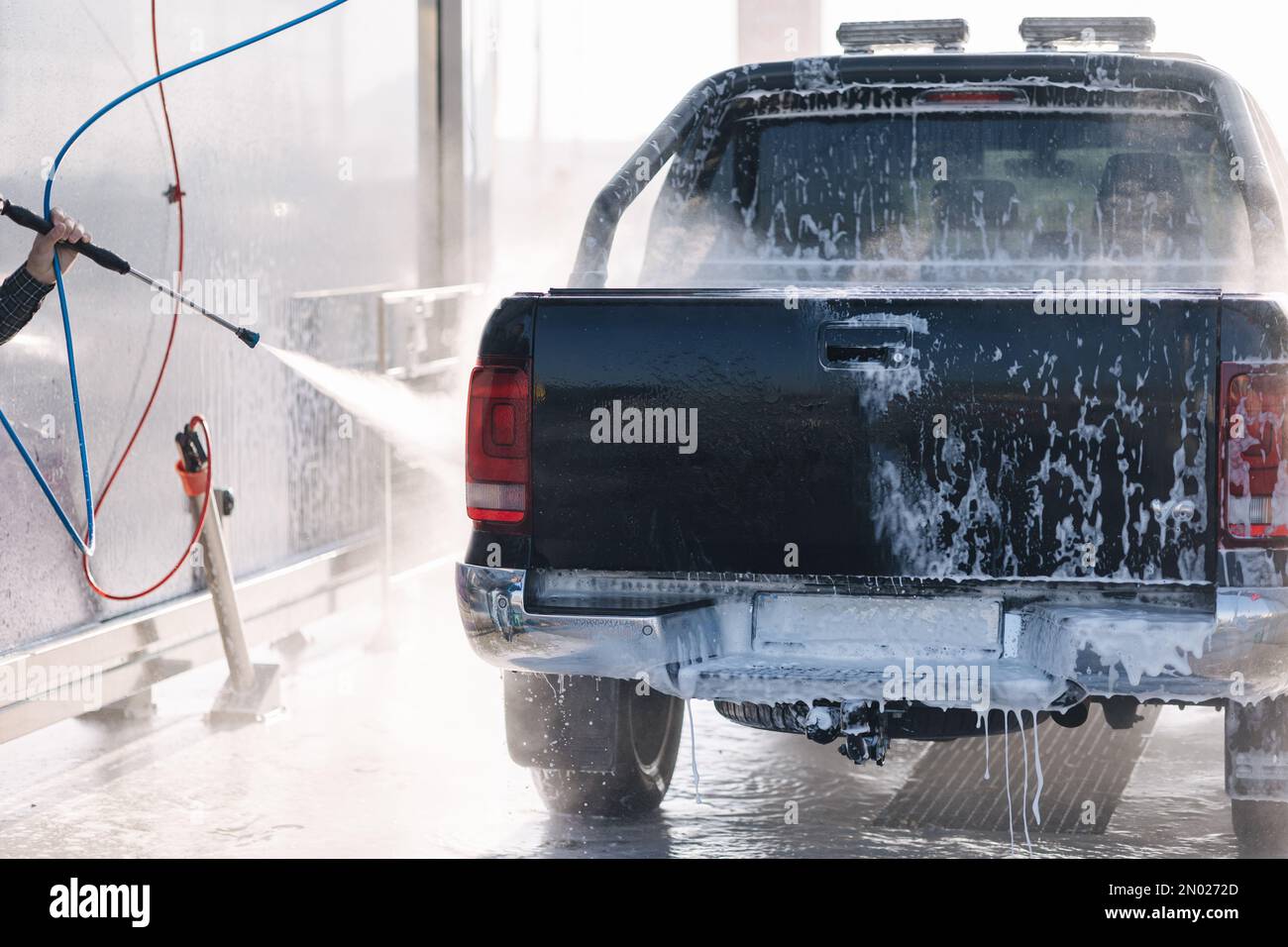 Process of man washing his car in a self-service car wash station. Back ...