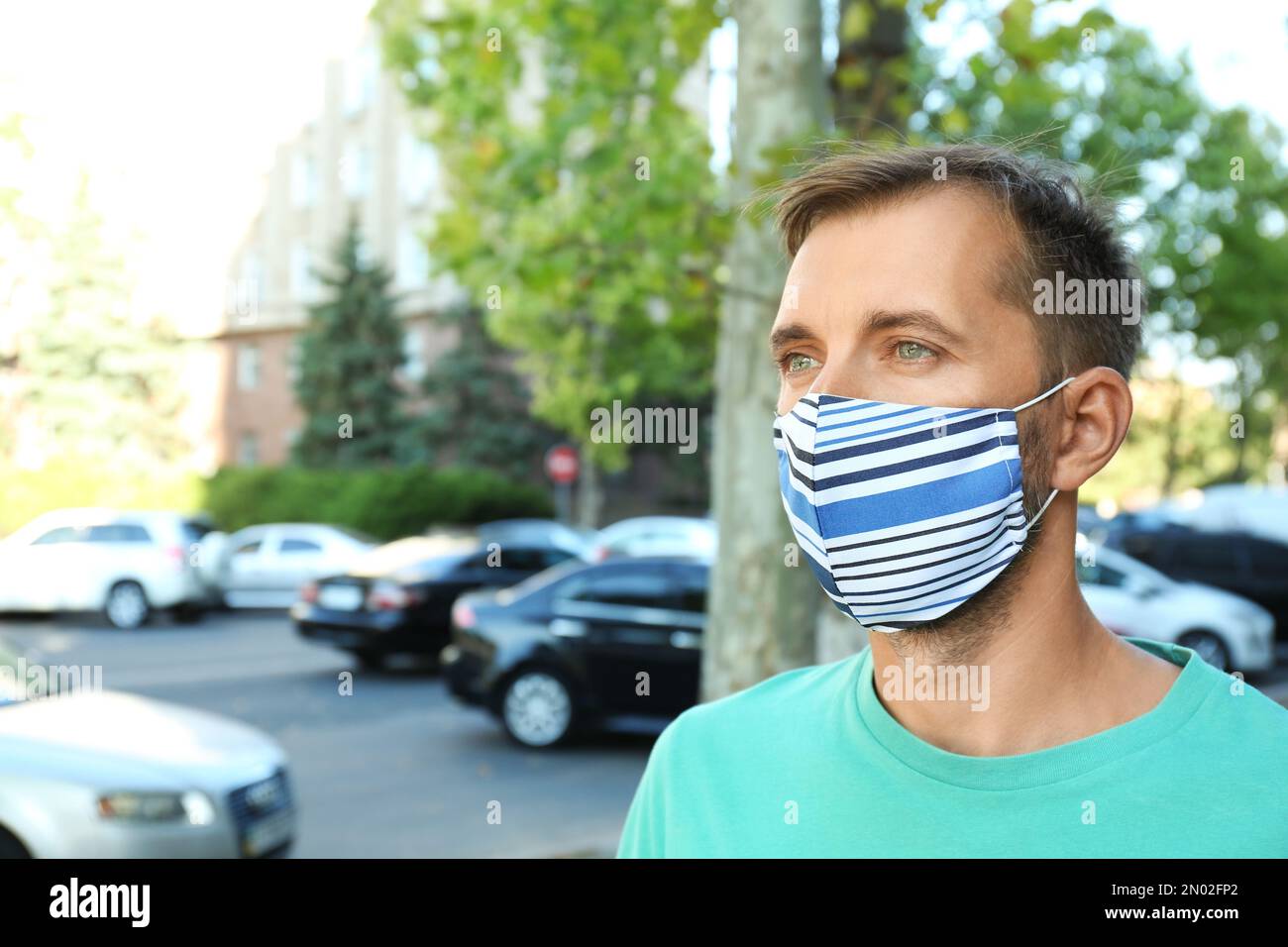 Man wearing handmade cloth mask outdoors, space for text. Personal ...