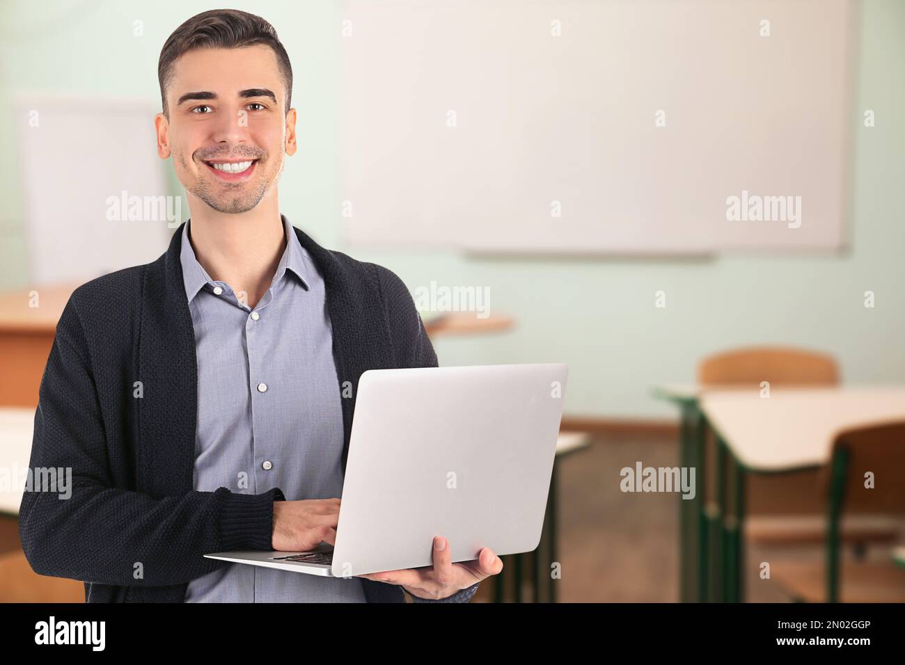 Young teacher with laptop waiting for students in classroom Stock Photo ...