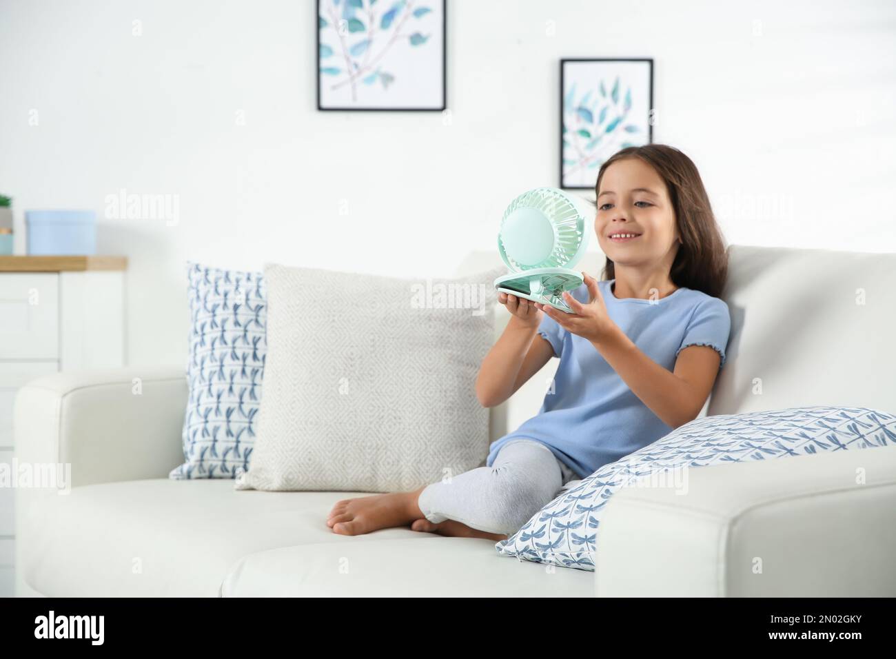 Little girl enjoying air flow from portable fan at home. Summer heat ...