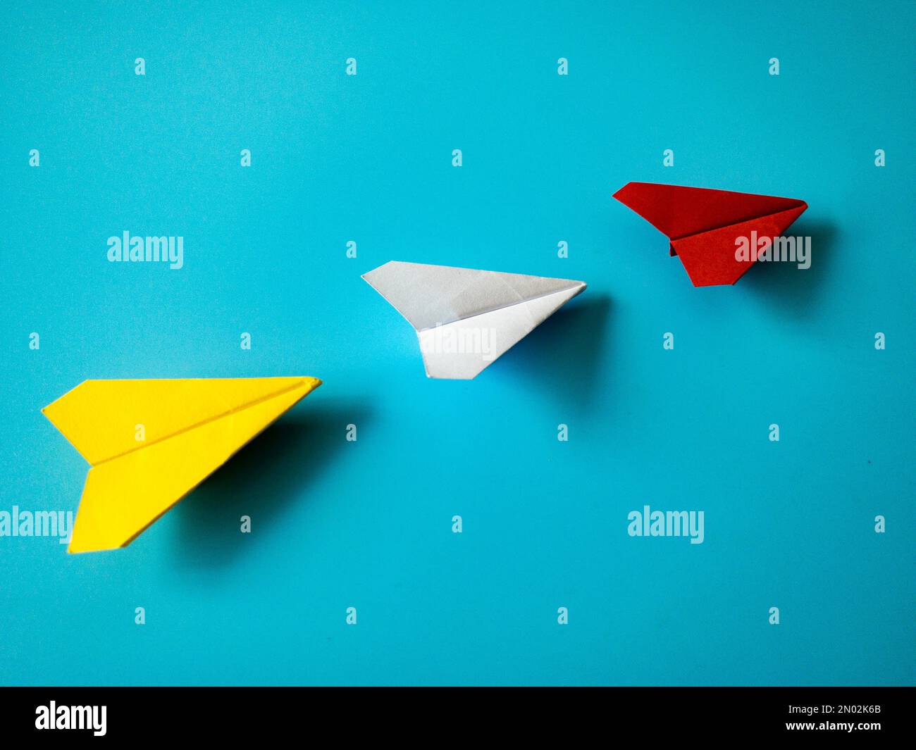 Red paper airplane origami leading white and yellow airplanes on blue ...
