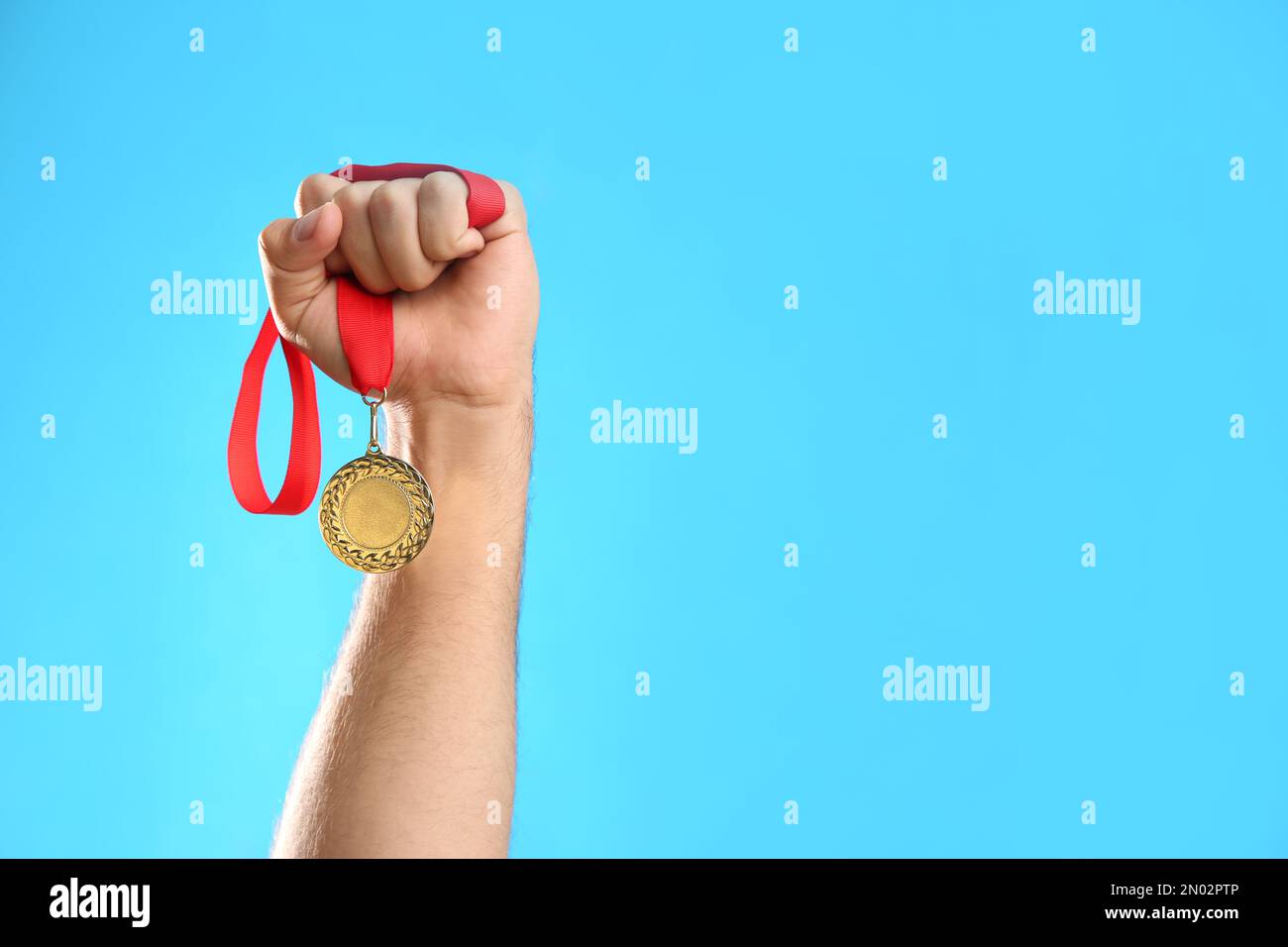 Man holding golden medal on light blue background, closeup. Space for ...