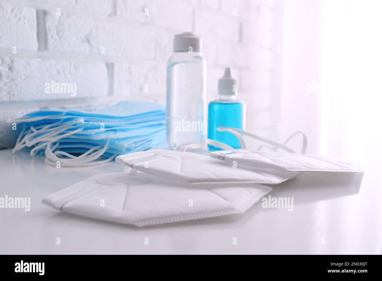 Hand sanitizers and respiratory masks on table near white brick wall ...