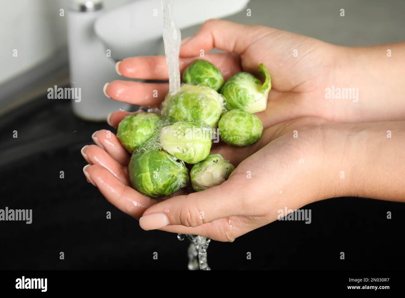 Woman washing Brussels sprouts with running water over sink, closeup ...