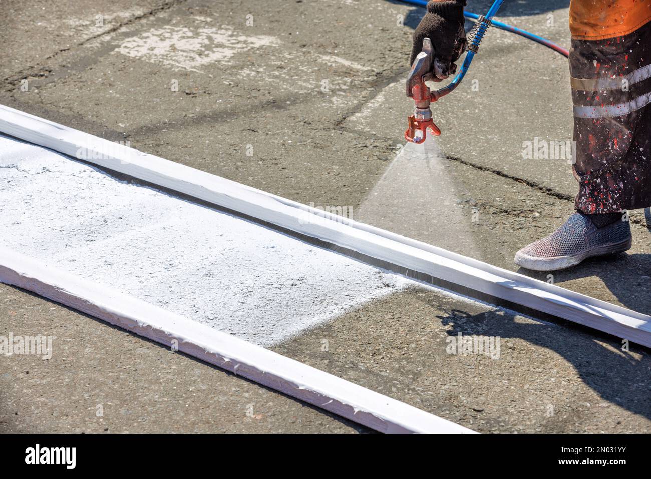 A road worker in dirty overalls applies white road markings with a ...