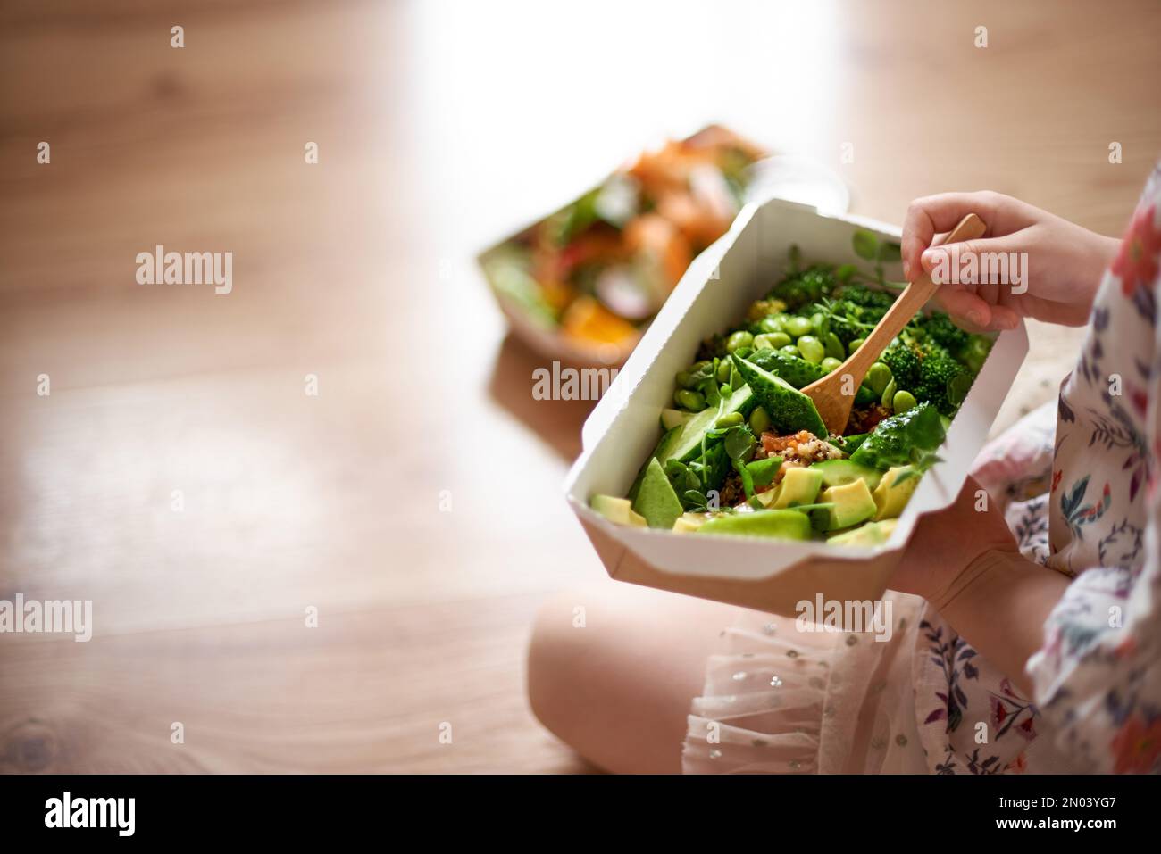 Paper container, food delivery concept. The girl eats a green salad of ...