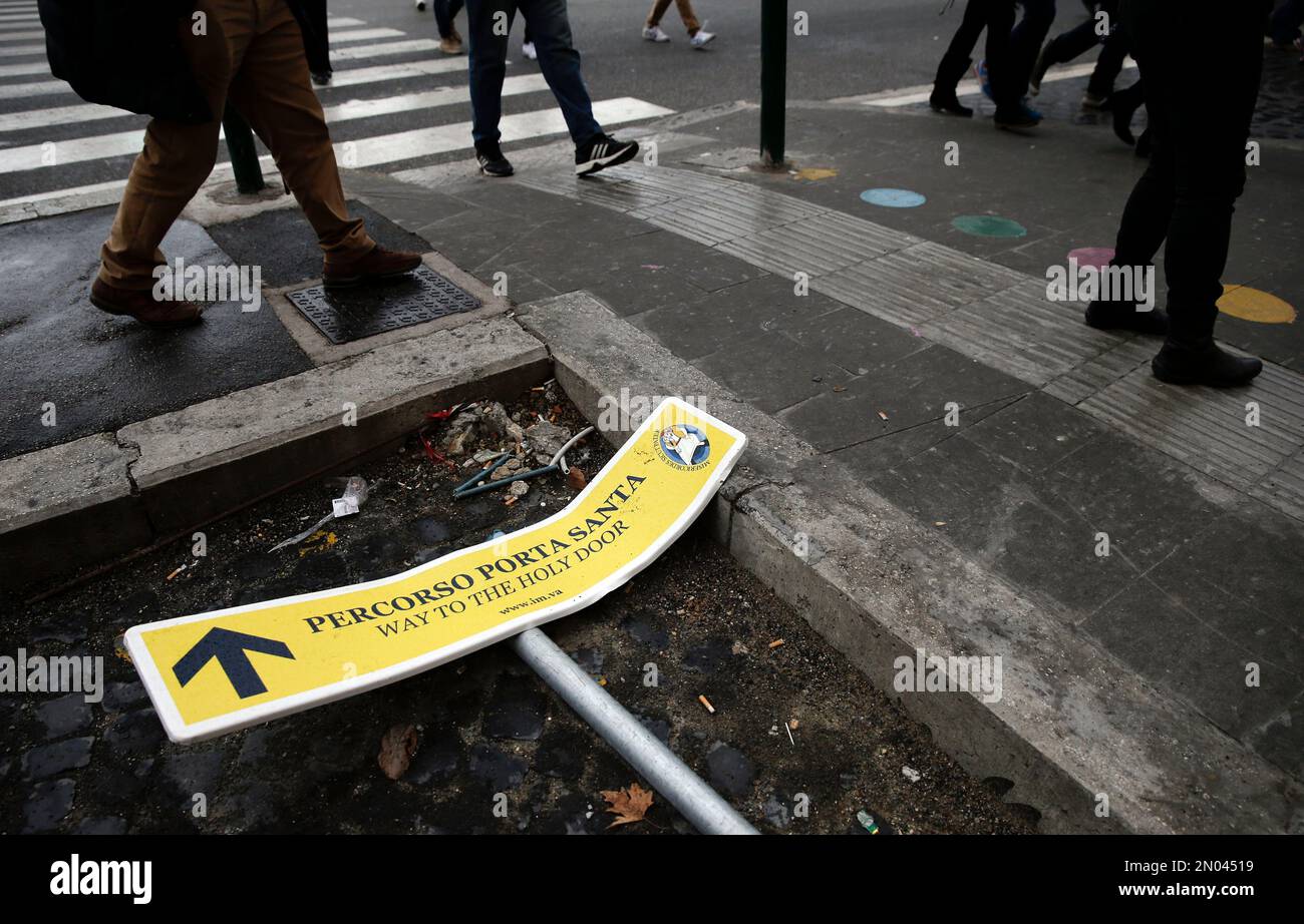 Pedestrians walk by a fallen street sign indicating the way to follow ...