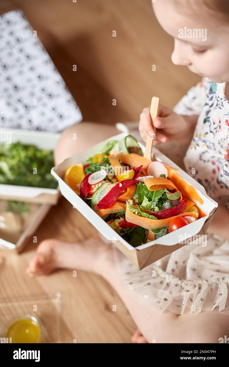 Paper container, food delivery concept. The girl eats a green salad of ...