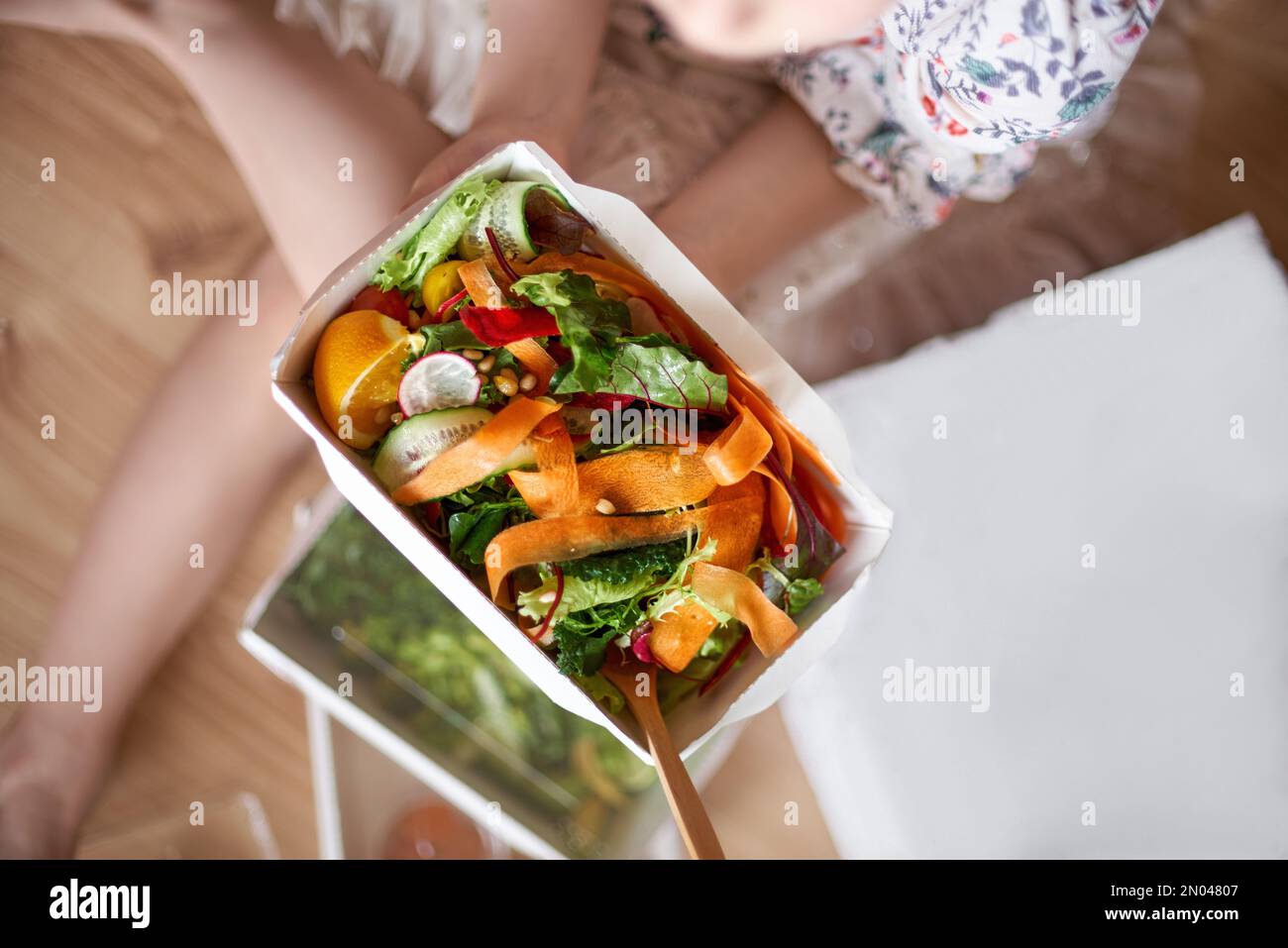 Paper container, food delivery concept. The girl eats a green salad of ...