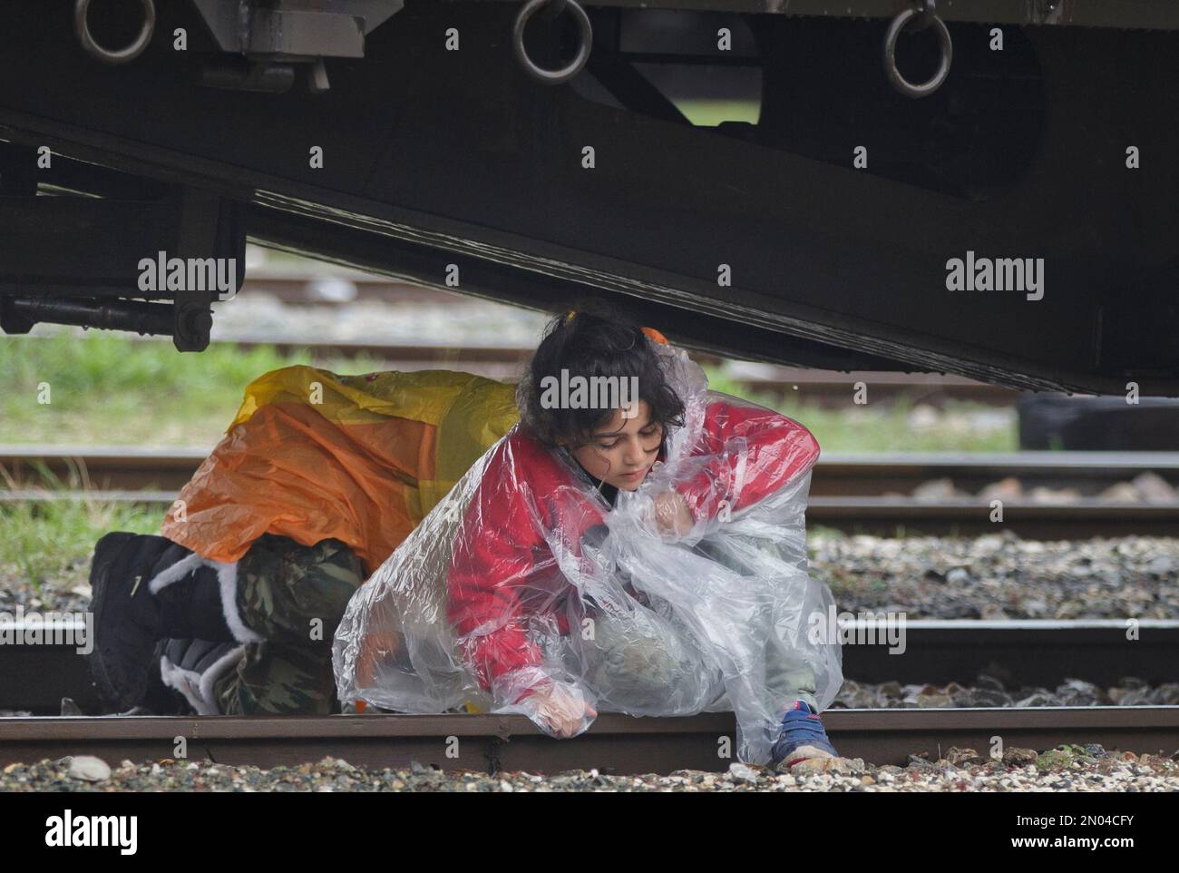 Migrant children cross railway tracks under a freight train during ...