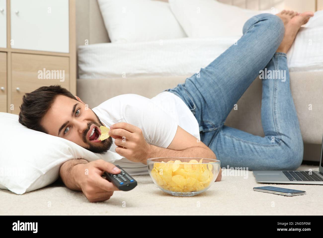 Lazy young man with bowl of chips watching TV while lying on floor at home Stock Photo - Alamy