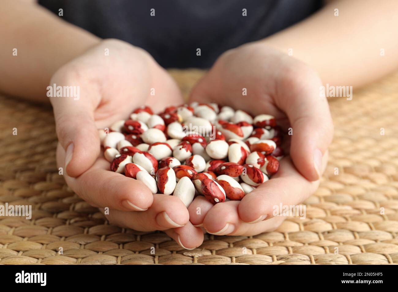 Woman holding pile of beans over wicker table, closeup. Vegetable seeds ...