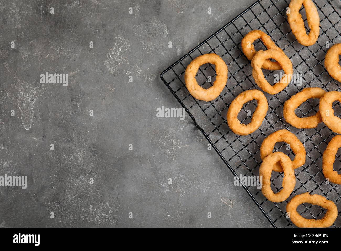 Cooling rack with fried onion rings on grey table, top view. Space for ...