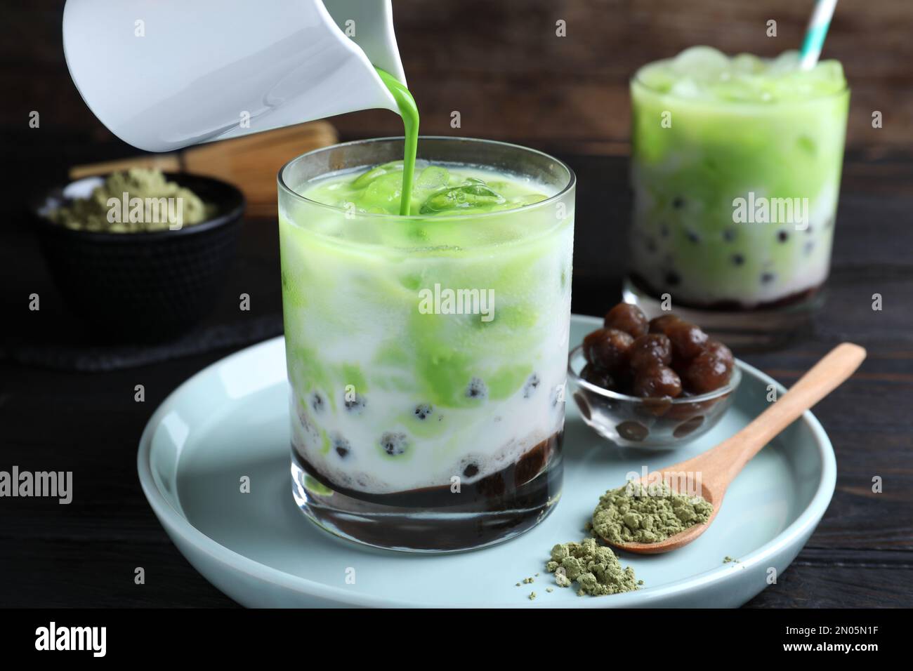 Pouring green matcha into glass with milk bubble tea at black wooden ...