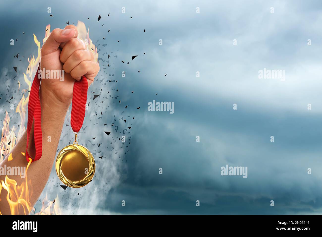 Winner raising hand with gold medal from fire flames up to stormy sky ...