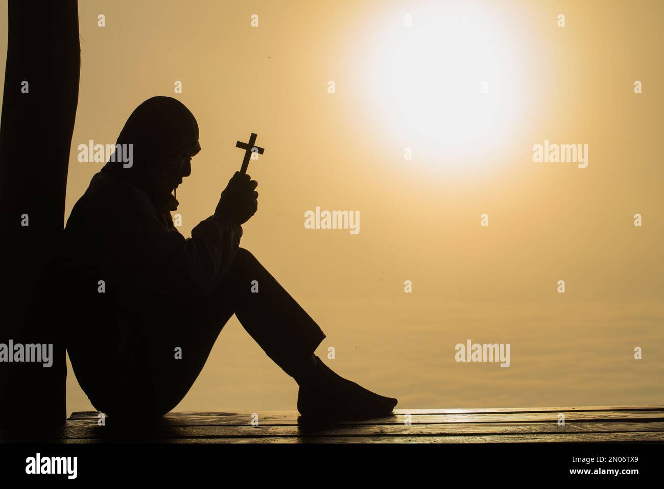 Silhouette of christian Man holding a cross cross in hands praying for ...