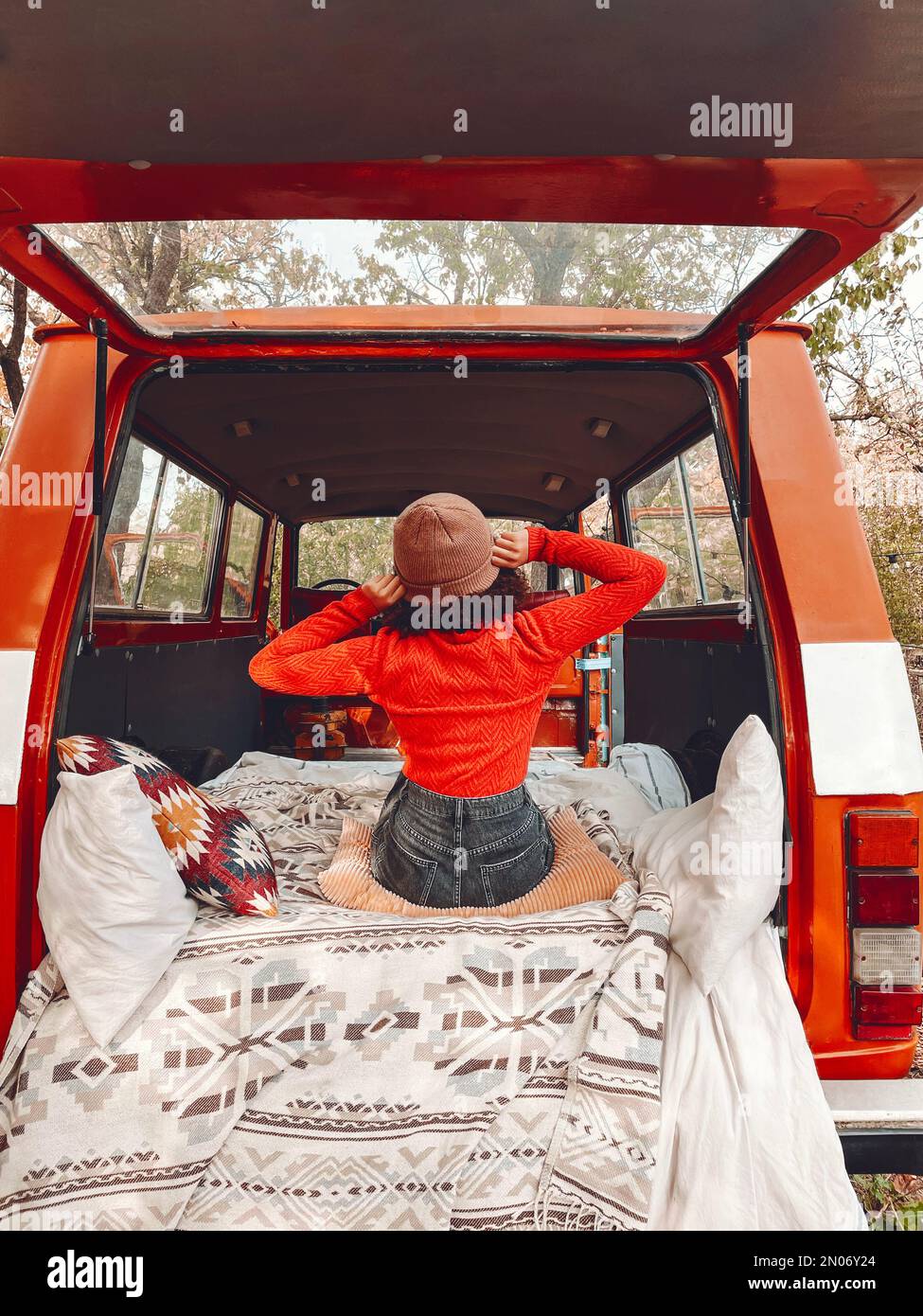 Rear view of young woman traveler sitting in minivan at campsite in ...