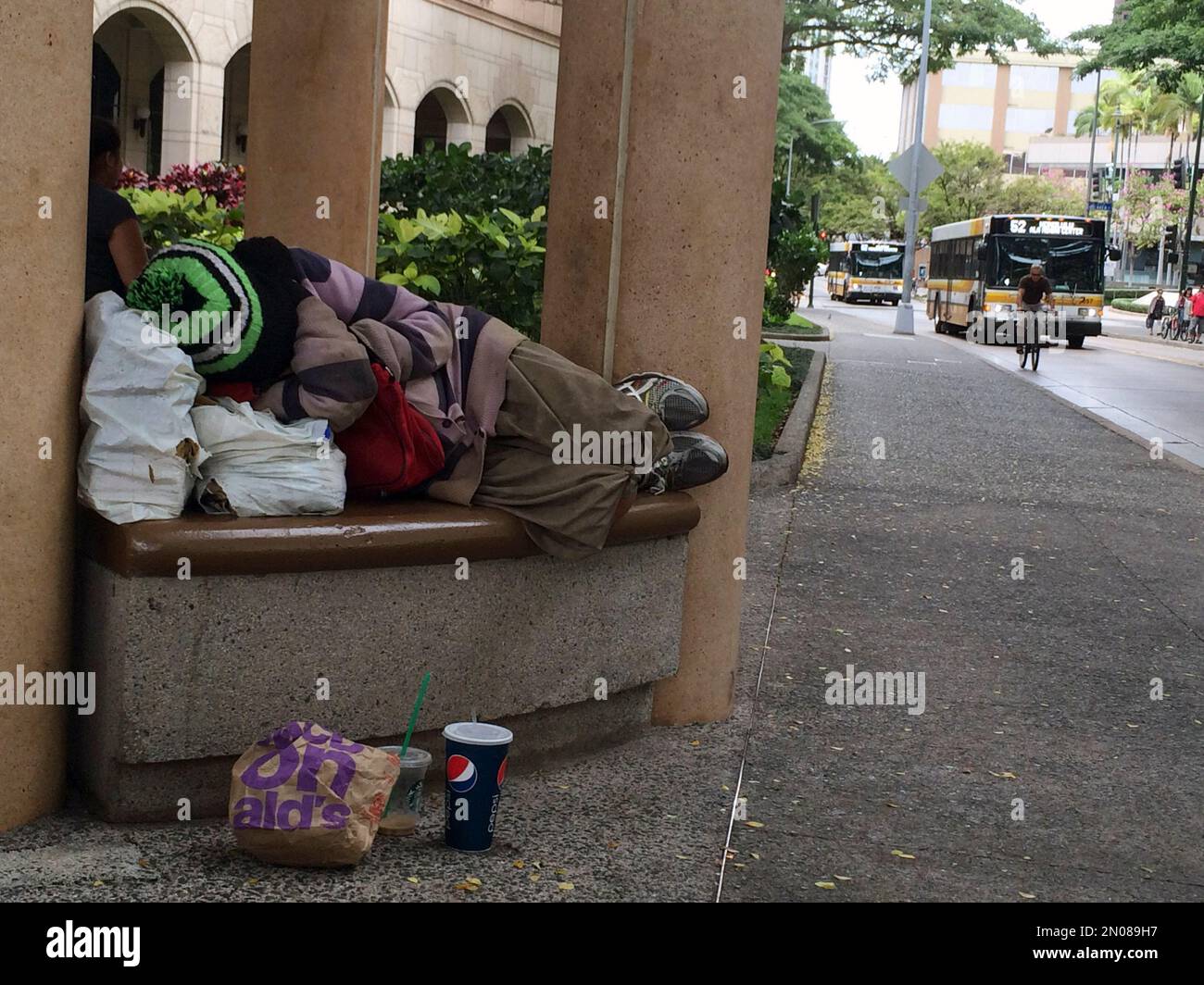 A person lies on a bench at a bus stop near the Hawaii state capitol on ...