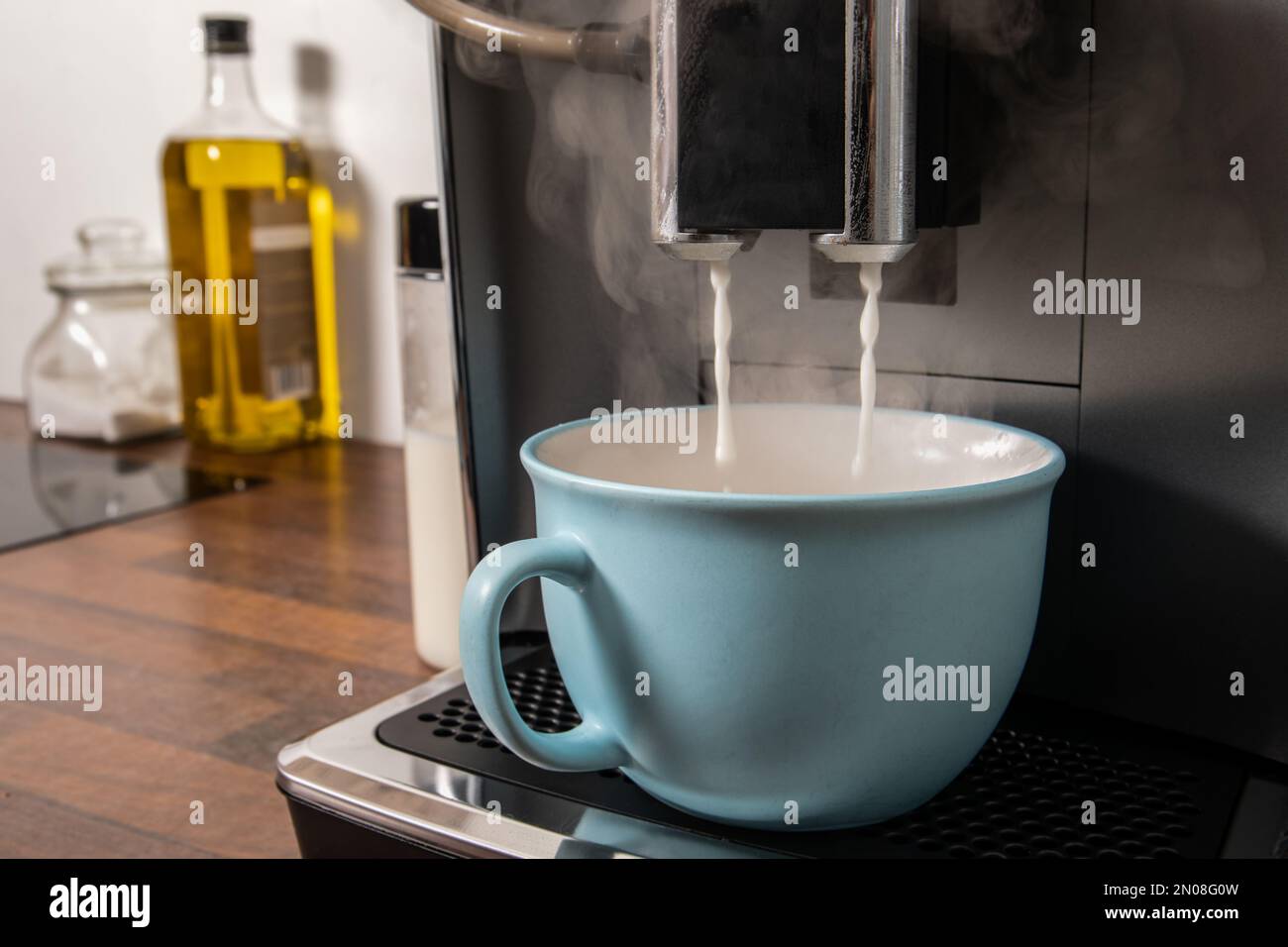 Making coffee. Milk flows from the coffee machine into a blue cup ...