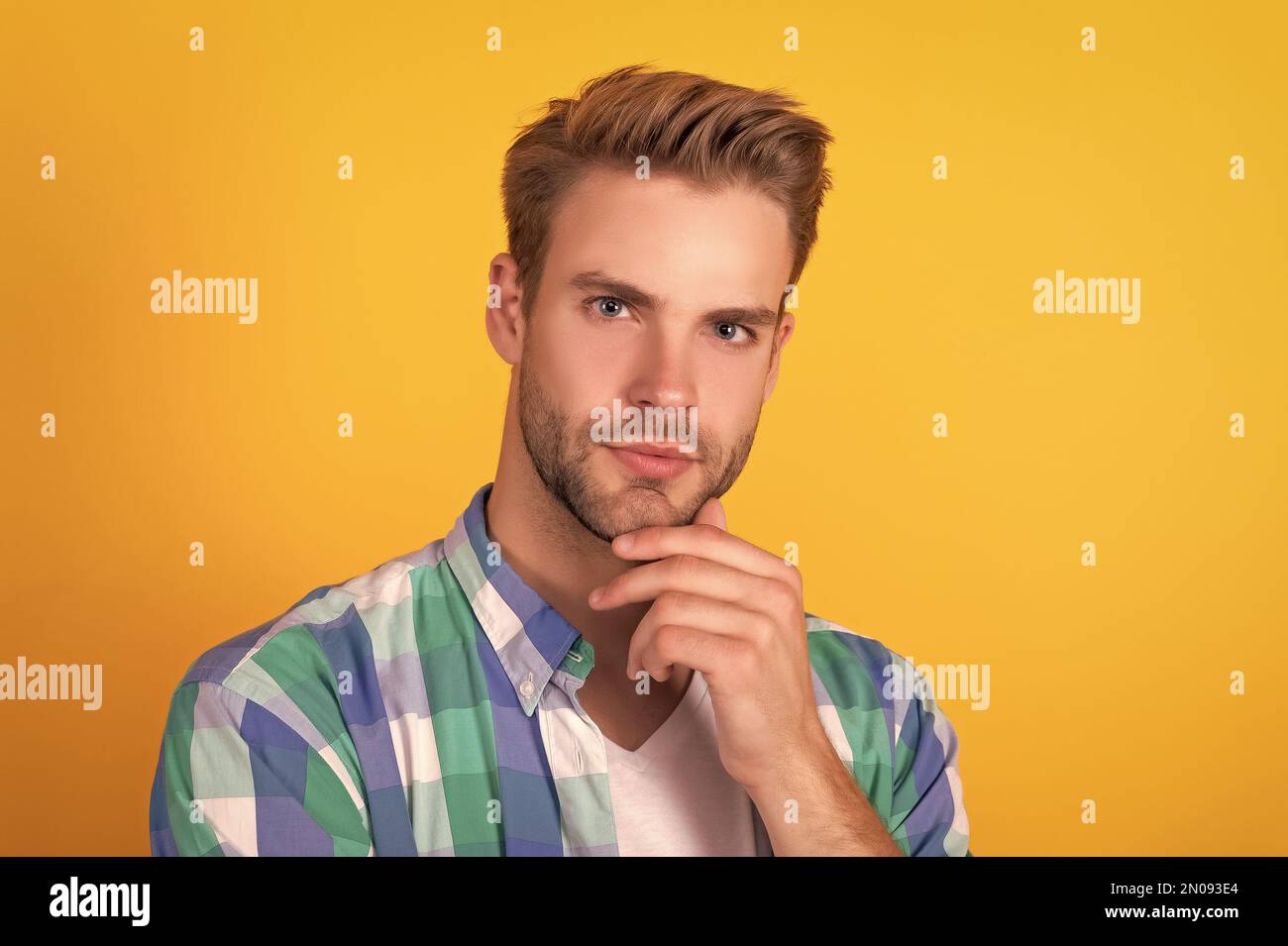 Handsome unshaven man portrait stroking chin with serious look yellow ...