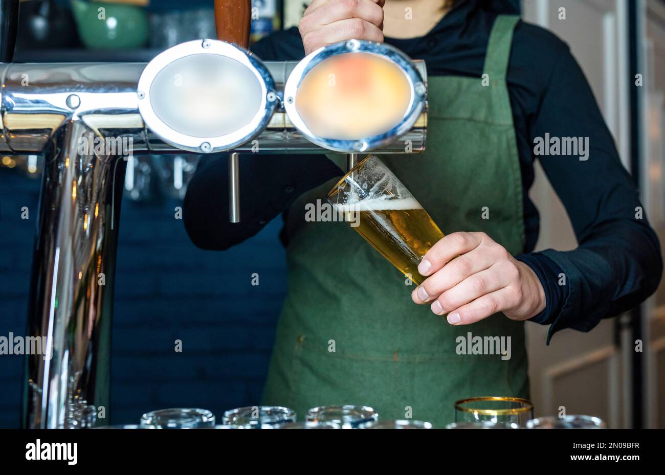 Female bartender tapping beer in bar, pouring from tap into the glass ...