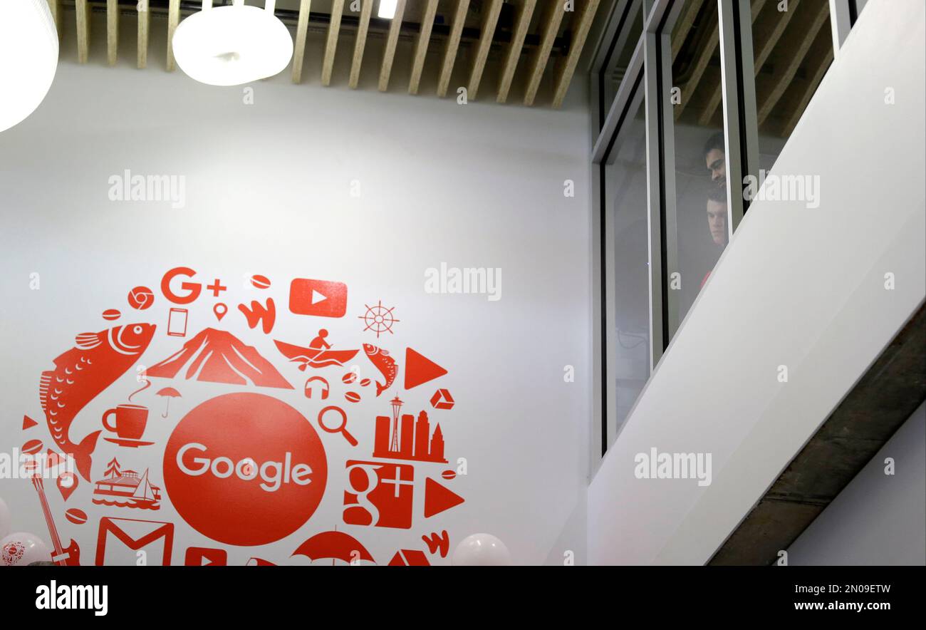 A pair of Google workers look down from an office into an open ...