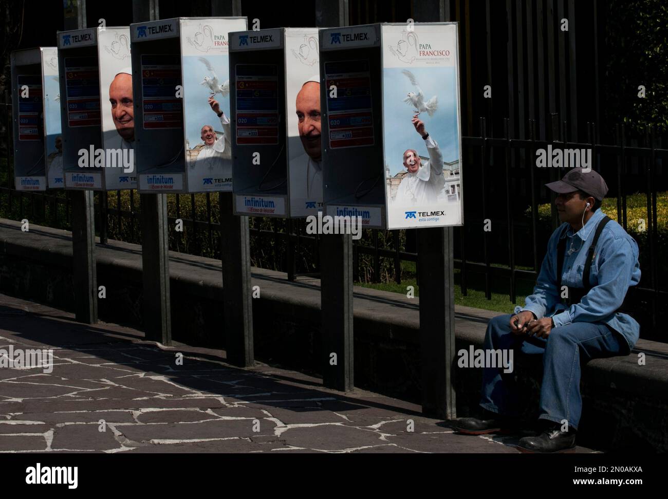 A man sits by public phone booths covered in images of Pope Francis ...