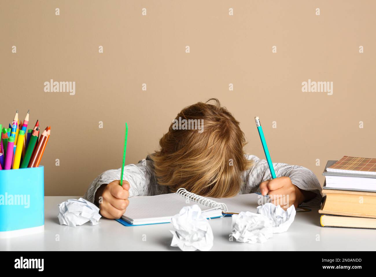 Tired little boy doing homework at table on beige background Stock ...