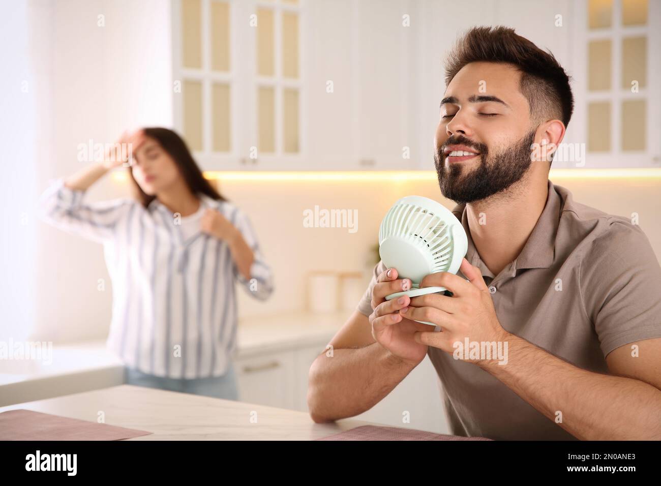 Man with portable fan enjoying cool air while his girlfriend suffering ...