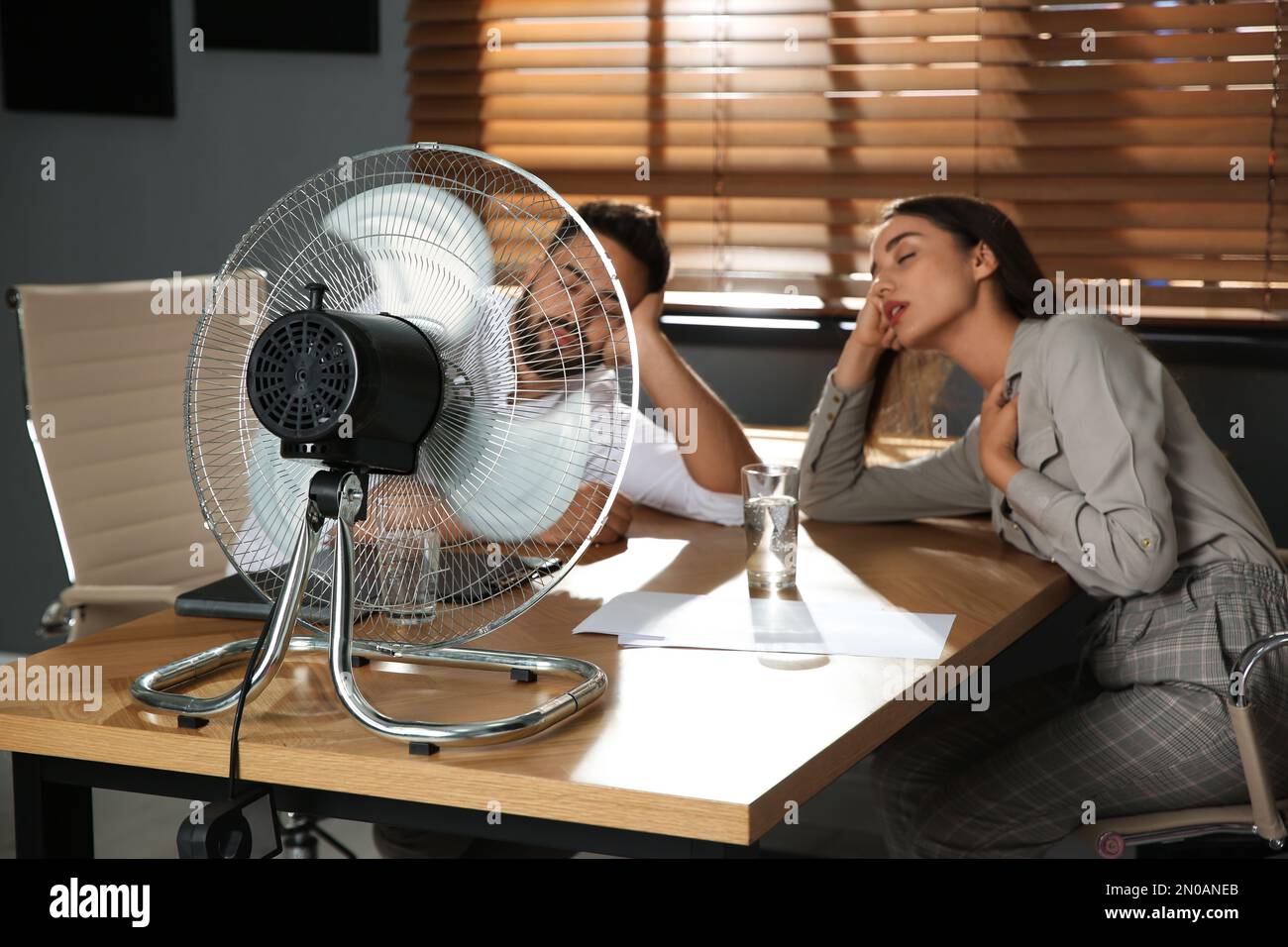 Office employees sitting in front of fan at workplace. Summer heat ...